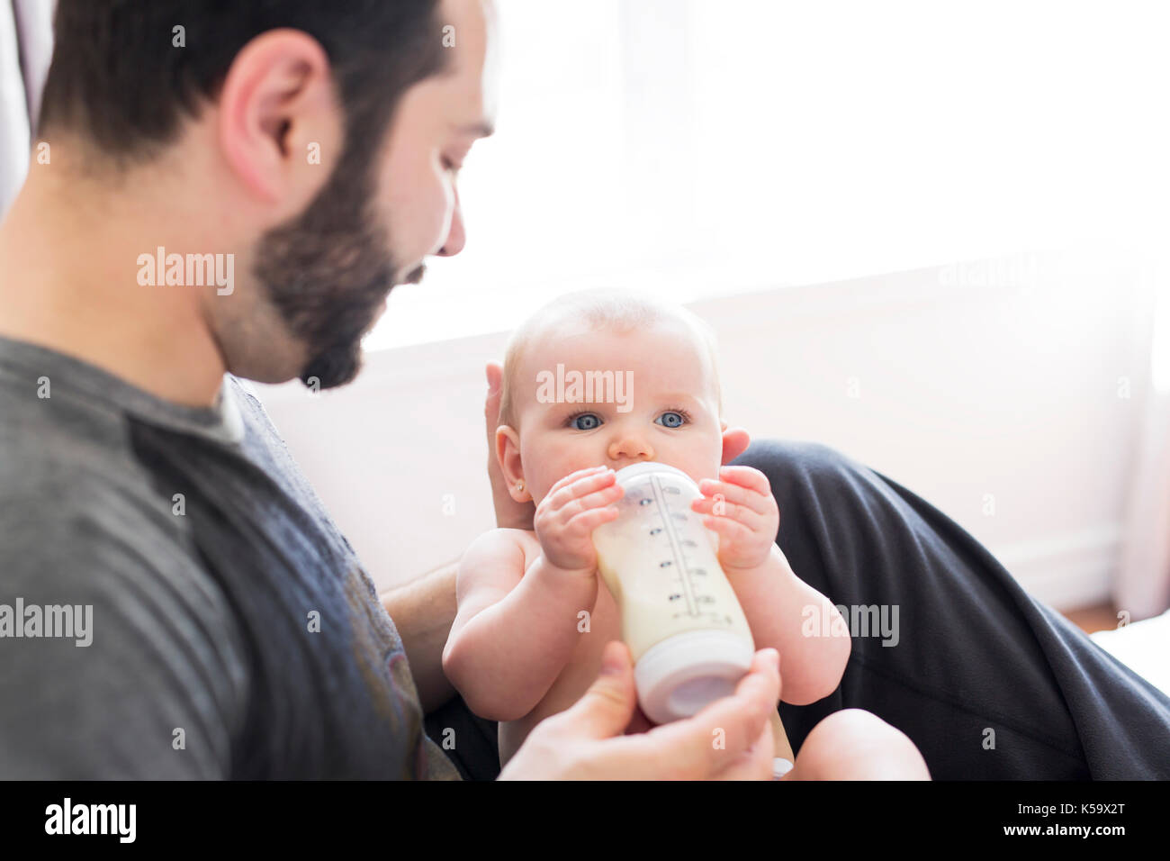 Happy man feeding milk to baby girl at home Stock Photo - Alamy