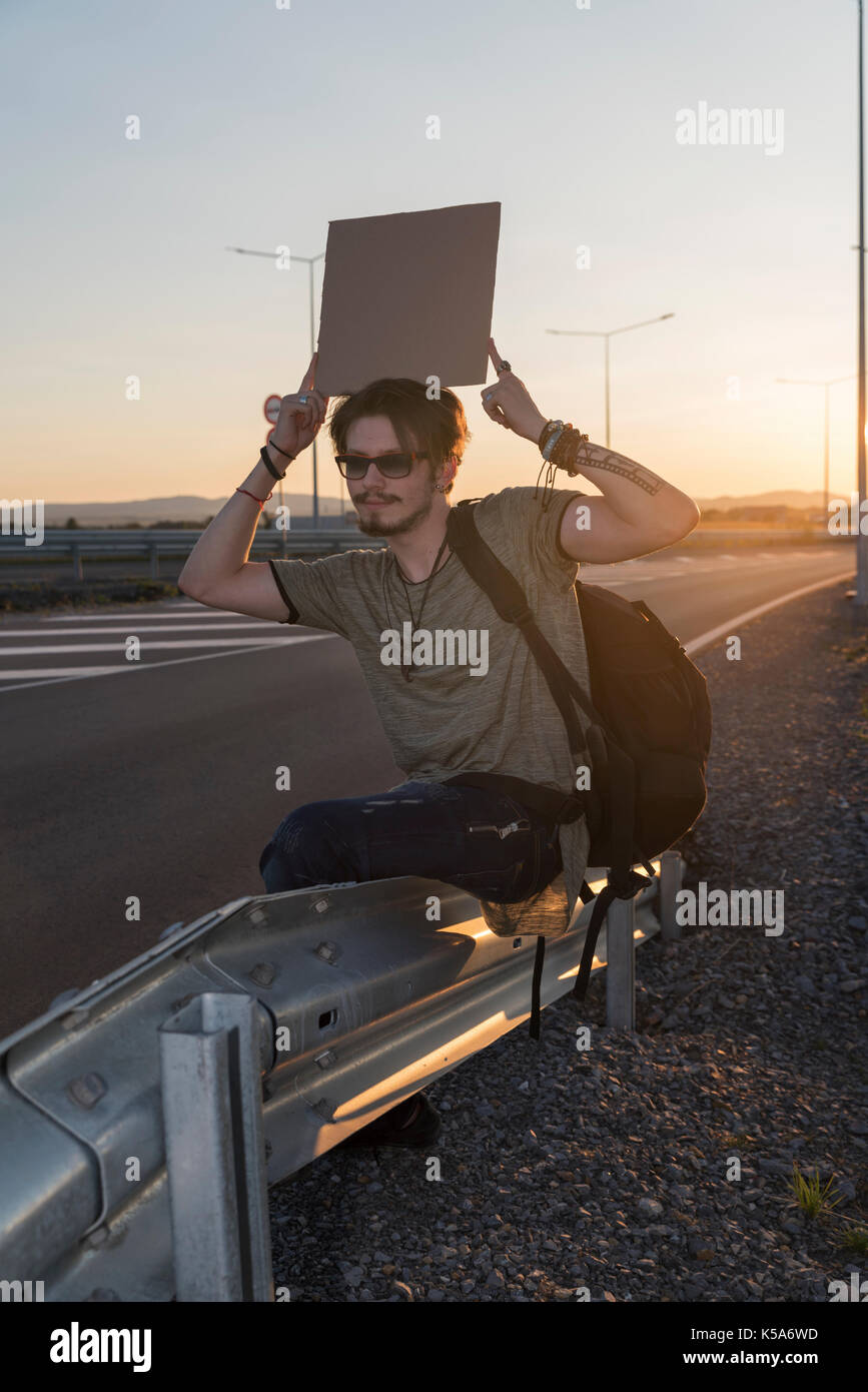 Smiling young man hitchhiking on a road Stock Photo - Alamy
