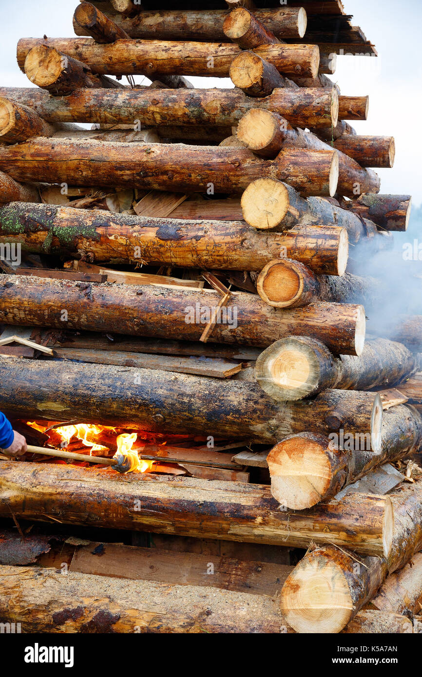 setting big bonfire made of logs on fire with torch Stock Photo - Alamy