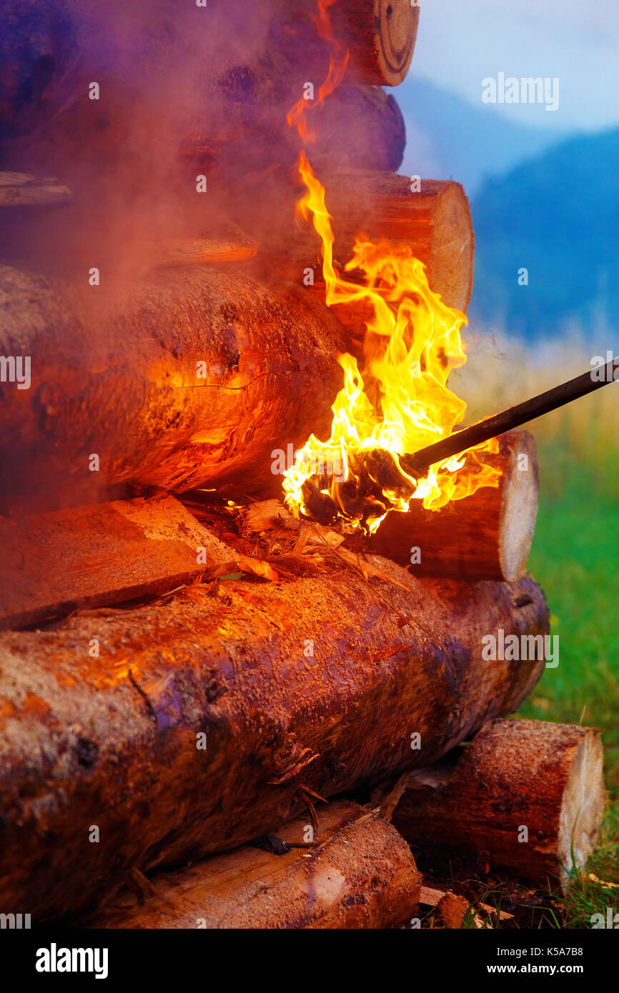 setting big bonfire made of logs on fire with torch Stock Photo - Alamy
