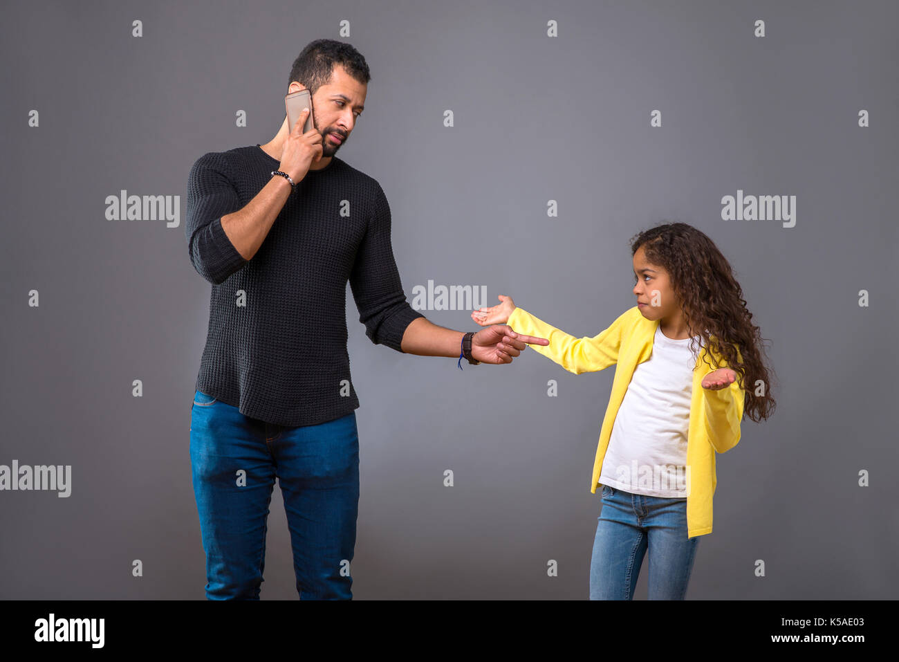 A black father talking on his phone while his young daughter looking at ...