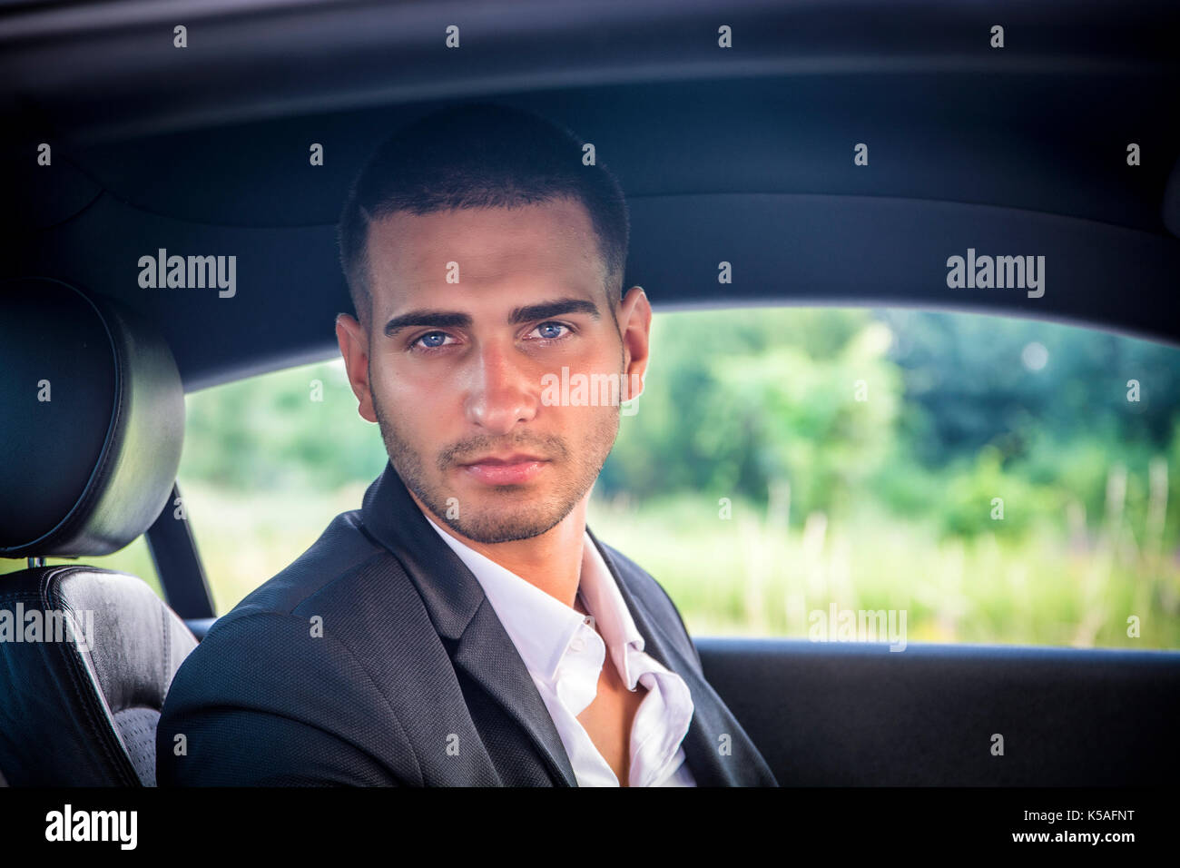 Handsome Young Man Driving a Car, wearing black jacket, hand on wheel ...