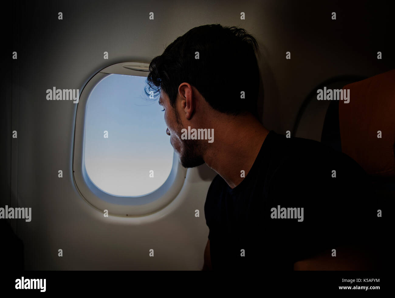 Side view of handsome young man against plane window sitting and ...