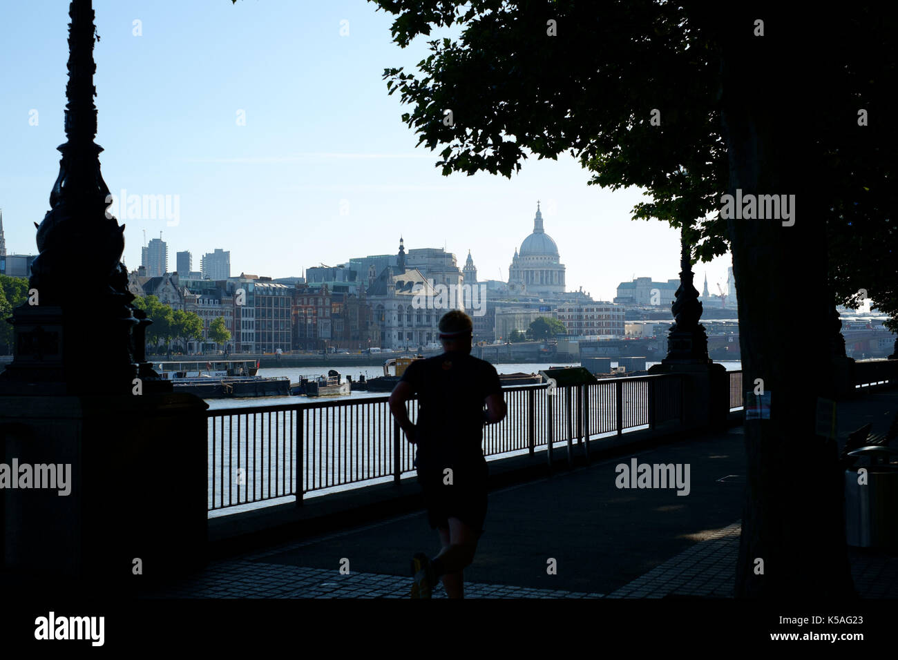 Man running along River Thames bank in shadow with St Paul's Cathedral ...