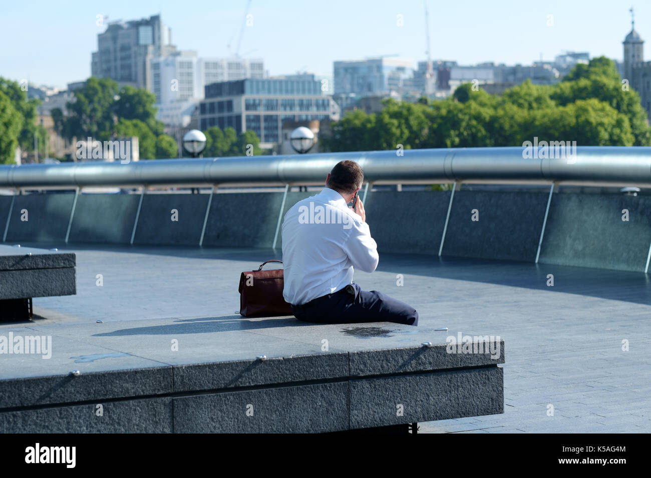 Business man sitting down outside on stone seating whilst using phone ...