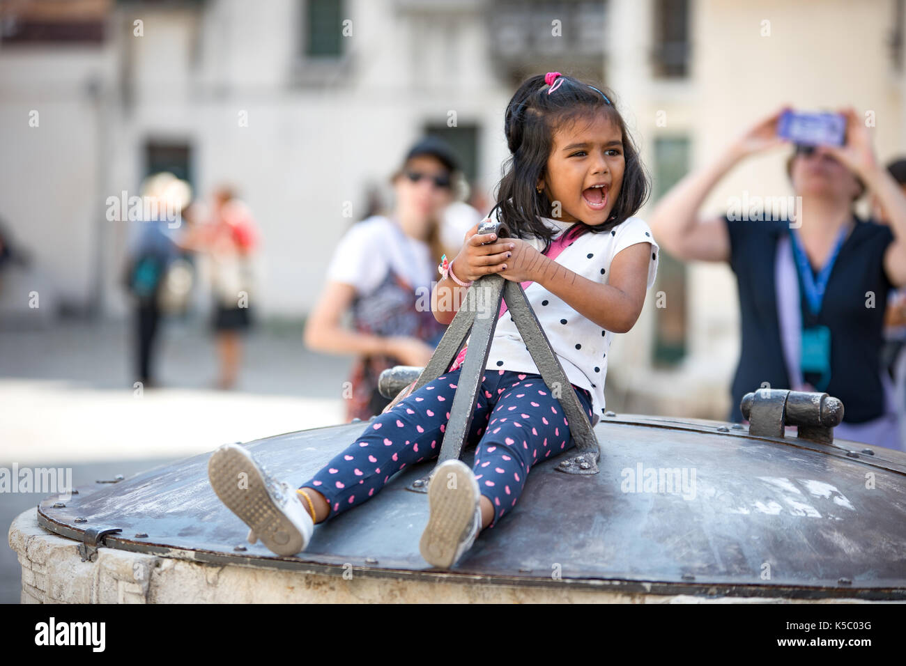 Little, beautiful black hair girl shouting out sitting on an old well ...