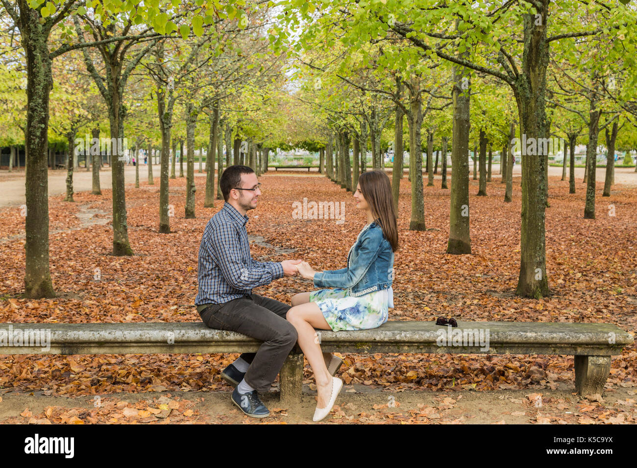 Lovely couple having fun together on a stone bench in a park in autumn ...