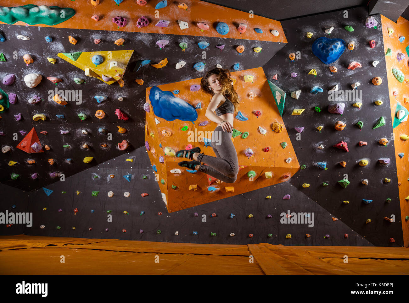 Pretty young woman jumping in climbing gym against wall with holds ...