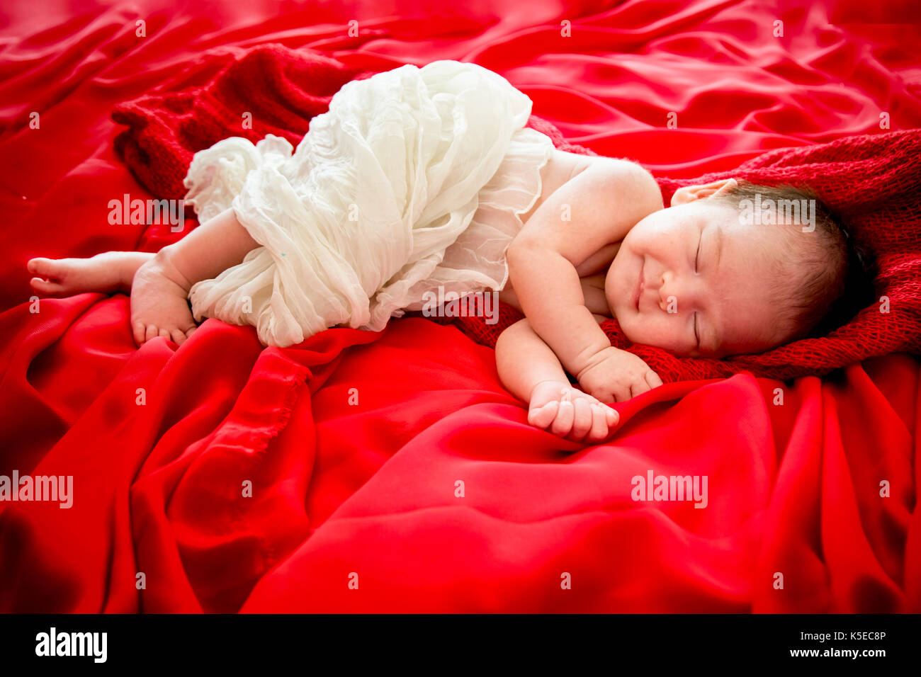 Newborn baby girl is sleeping on red fabric blanket Stock Photo - Alamy