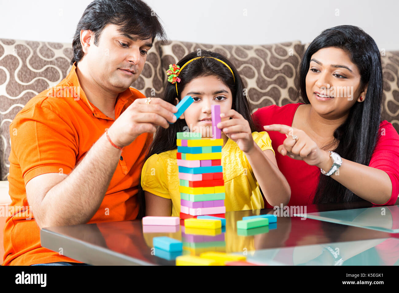 Parents helping her Little daughter build tower from colorful building ...