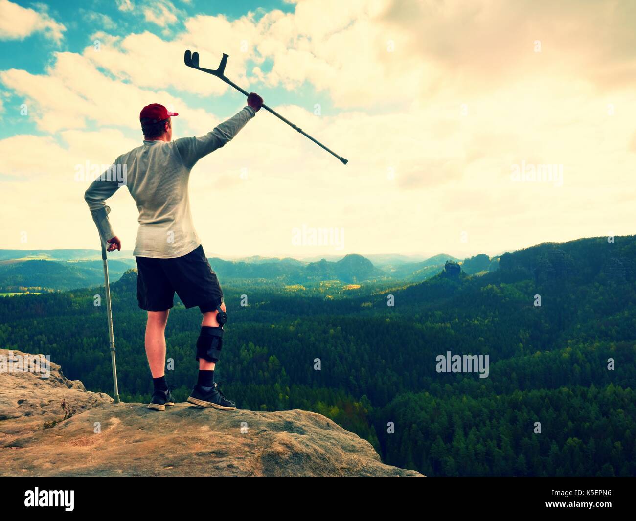Happy tourist with forearm crutch above head achieved mountain peak ...