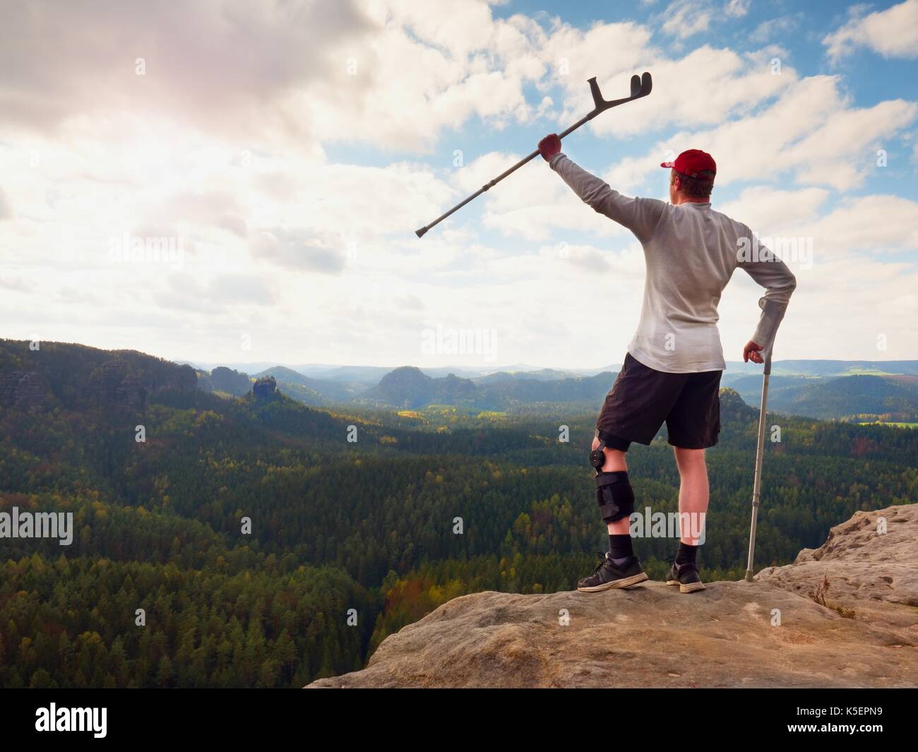 Happy tourist with forearm crutch above head achieved mountain peak ...
