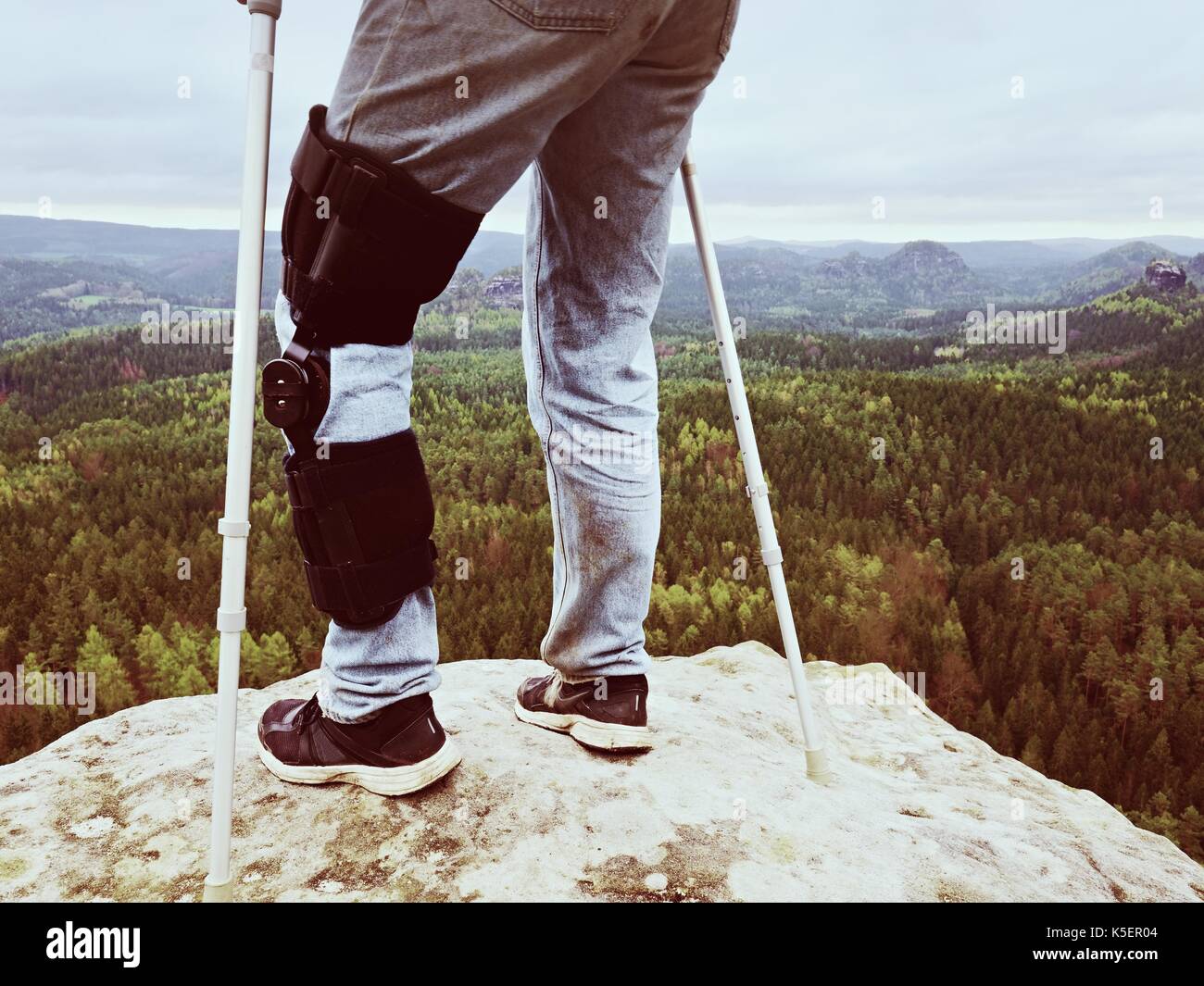 Man with leg in knee cages and crutches for stabilization stay on rock ...