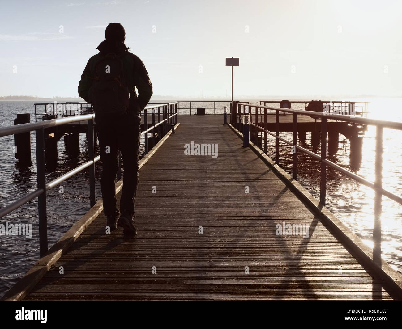 Man tourist at wooden sea pier. Cold windless morning with gradient ...