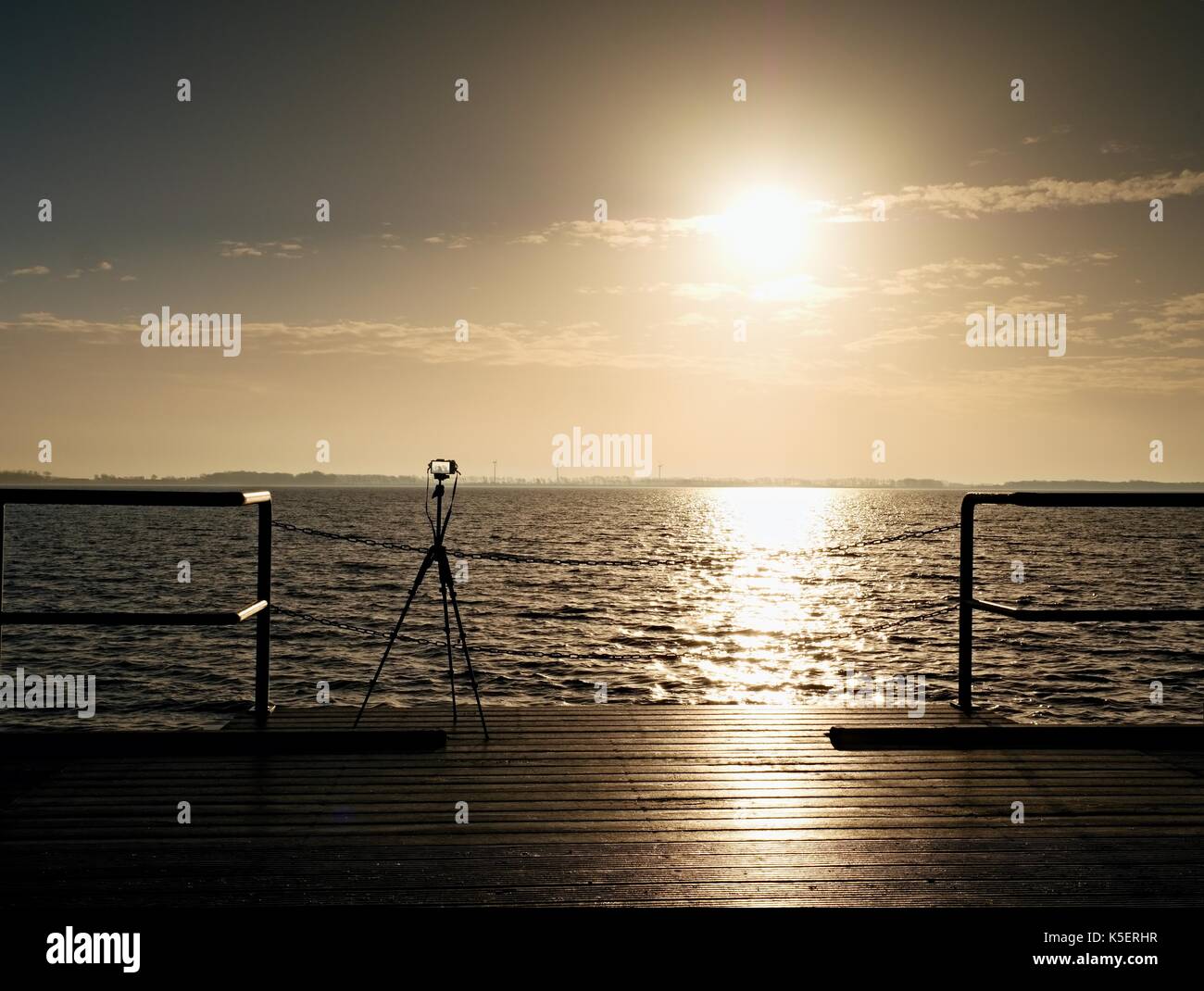 Tripod with camera ready on pier, Sun above ocean. Empty wooden mole ...