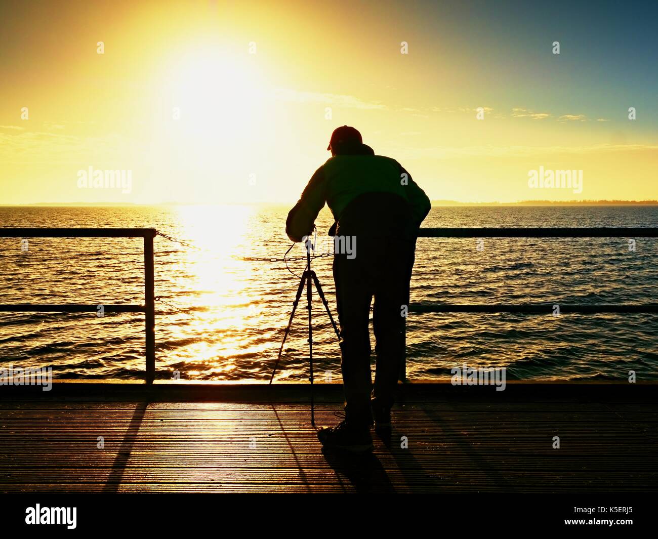 Hunched professional photograph work at sea. Tourist on wooden wharf ...