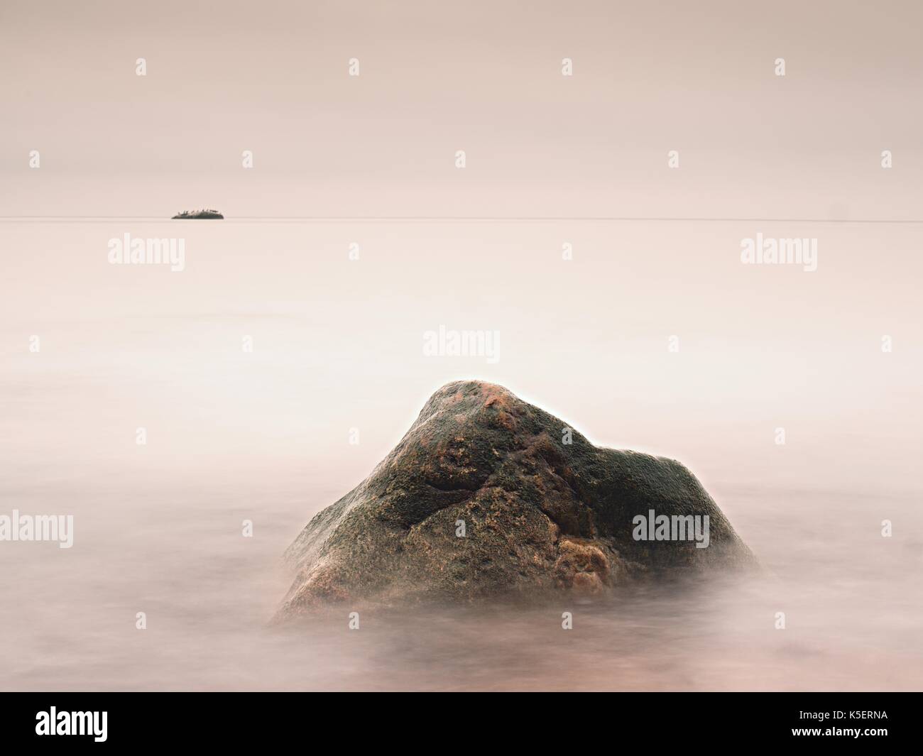 Romantic sea. Boulder stick out from smooth wavy sea. Pink horizon ...