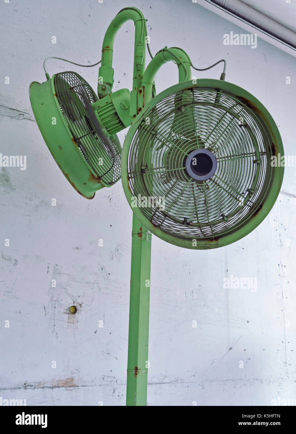 two green air fans stand against a white wall on the sidewalk of Miami ...