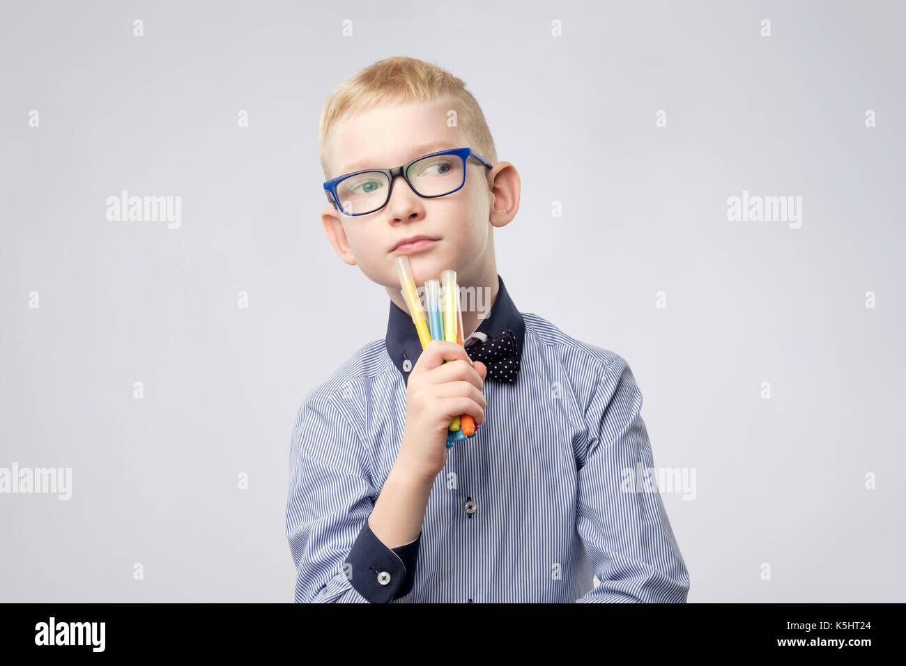 Caucasian boy with blond hair holding pencils in hands and looking up ...