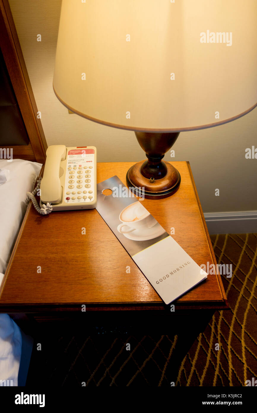 A room service menu placed on bedside lamp stand cabinet in hotel room ...