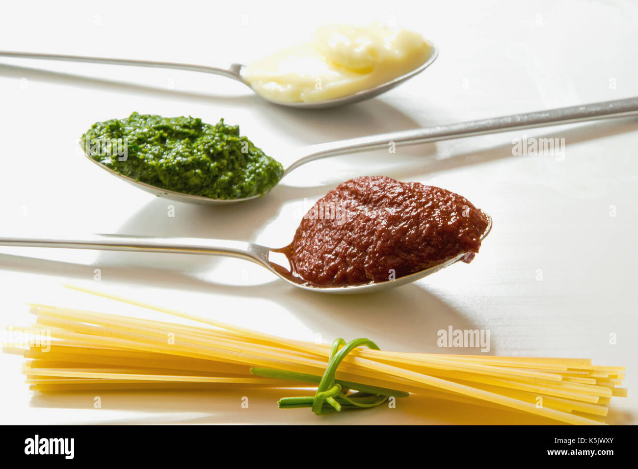Spaghetti and three spoons with different condiments - tomato sauce ...
