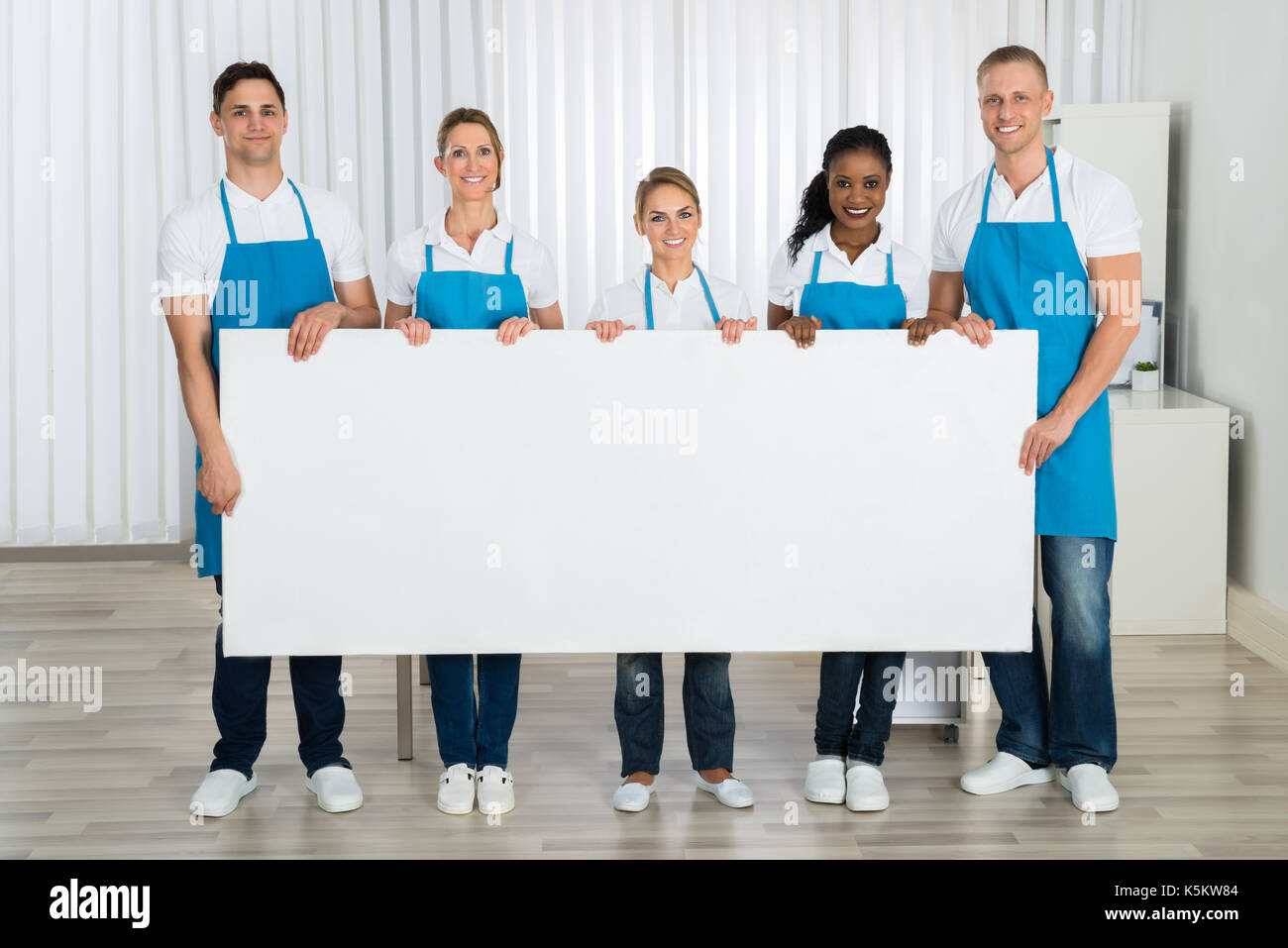 Group Of Happy Cleaners In Uniform Holding Blank Banner In Office Stock ...
