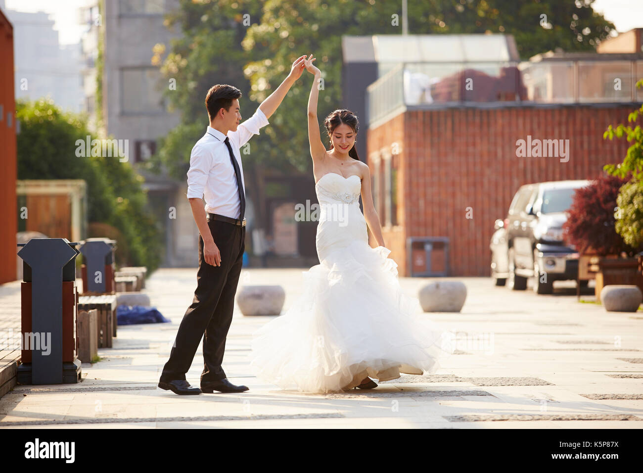 young asian bride and groom in wedding dress dancing in parking lot ...