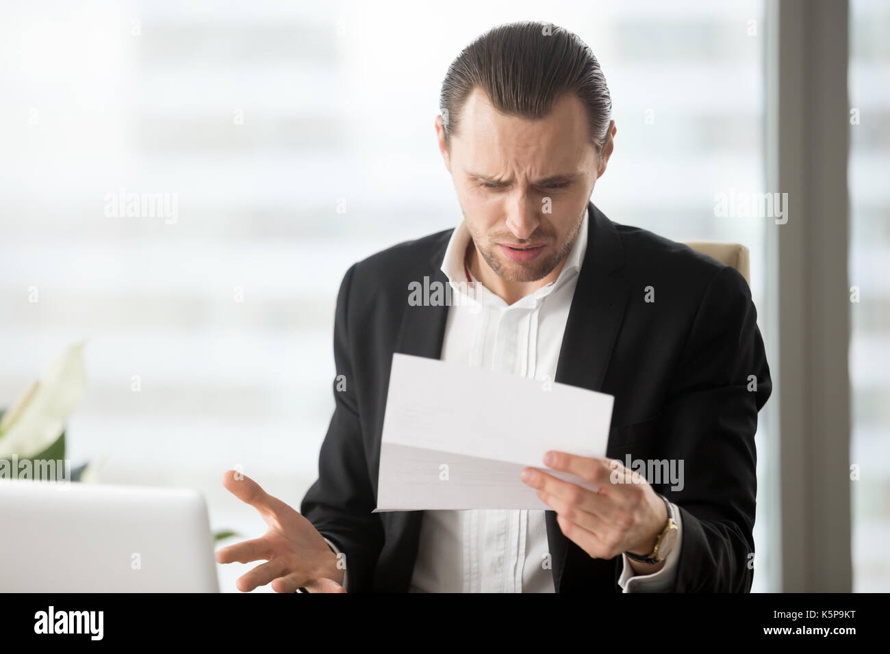 Frustrated young businessman looking at confusing letter in offi Stock ...
