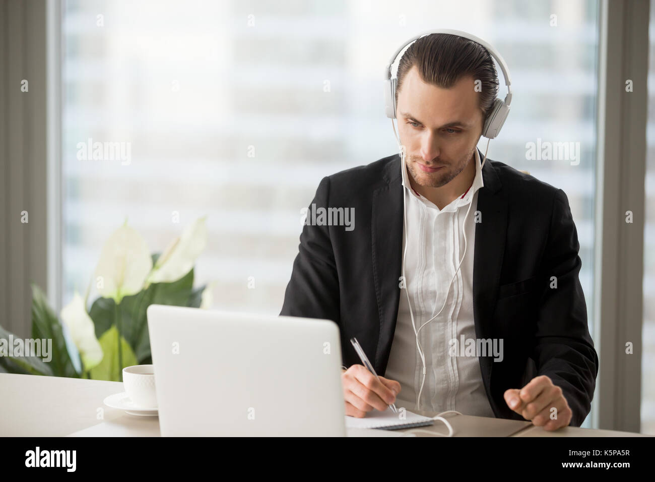 Businessman in headphones taking notes in front of laptop Stock Photo ...