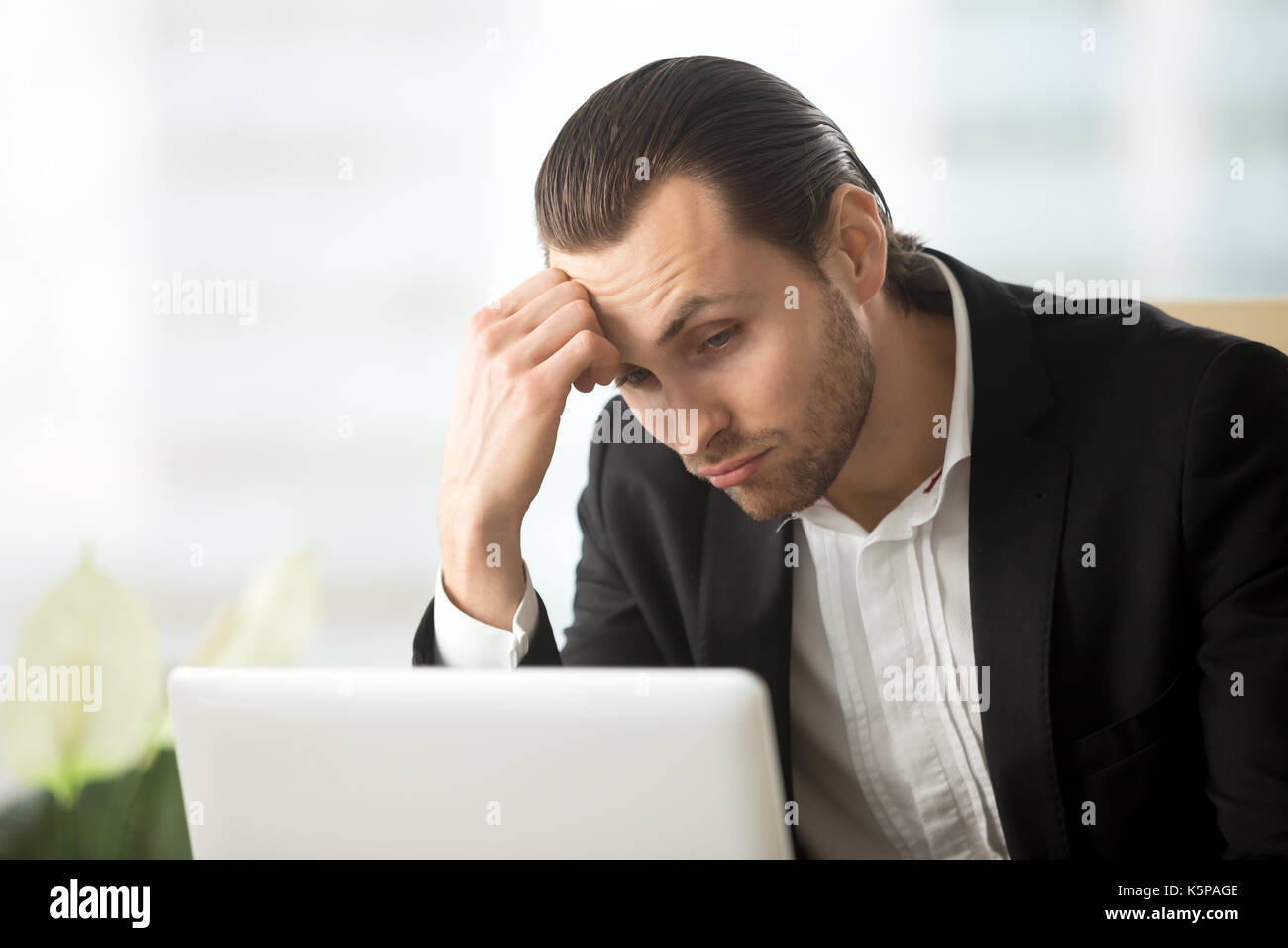 Puzzled young businessman looking at laptop screen at workplace Stock ...