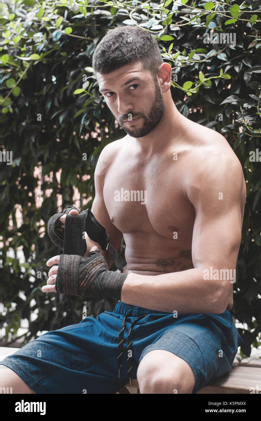 Muscular male boxer wraps his hands in bandages looking at camera Stock ...