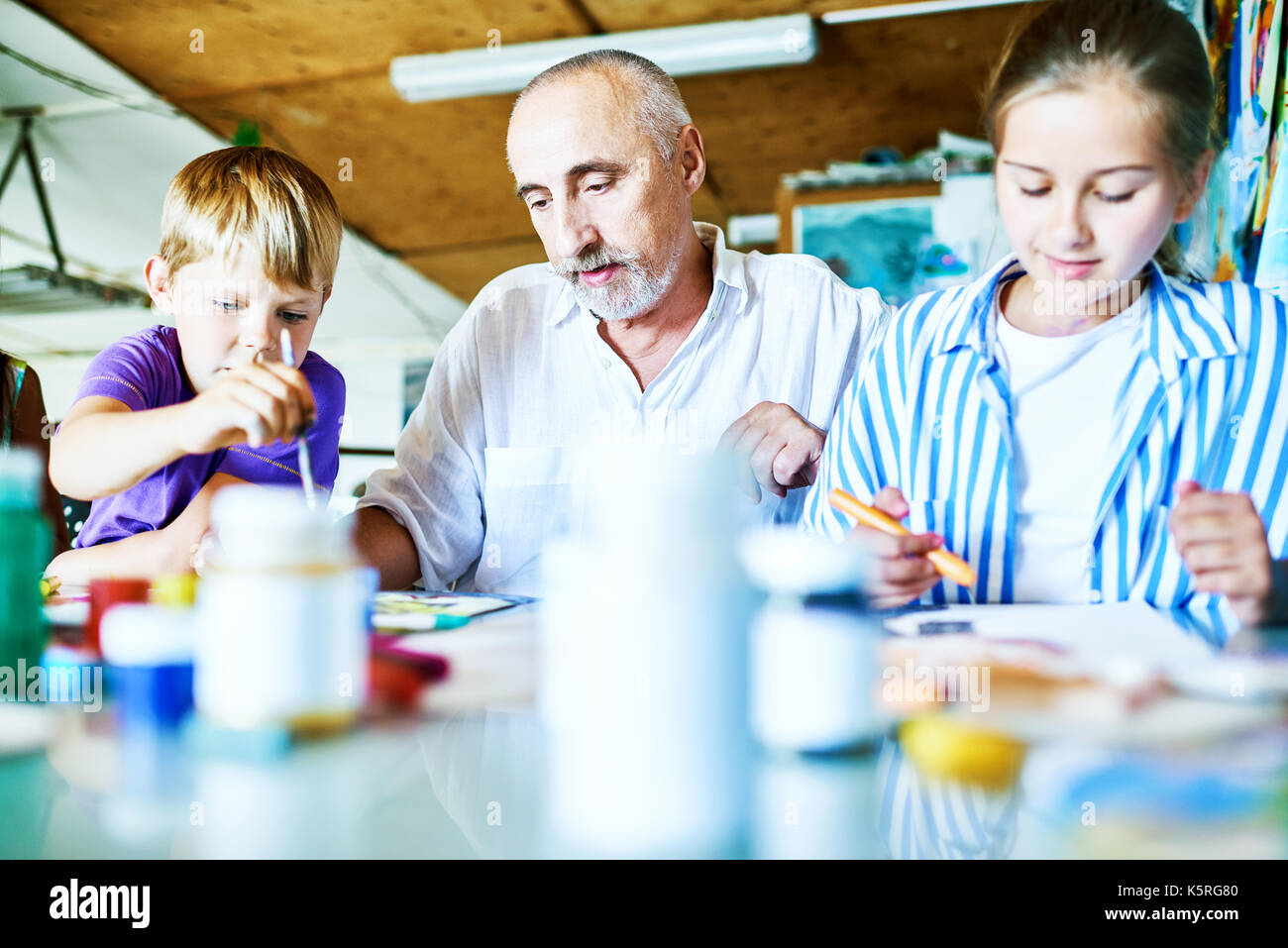 Mature drawing teacher giving lesson to his little pupils while sitting ...