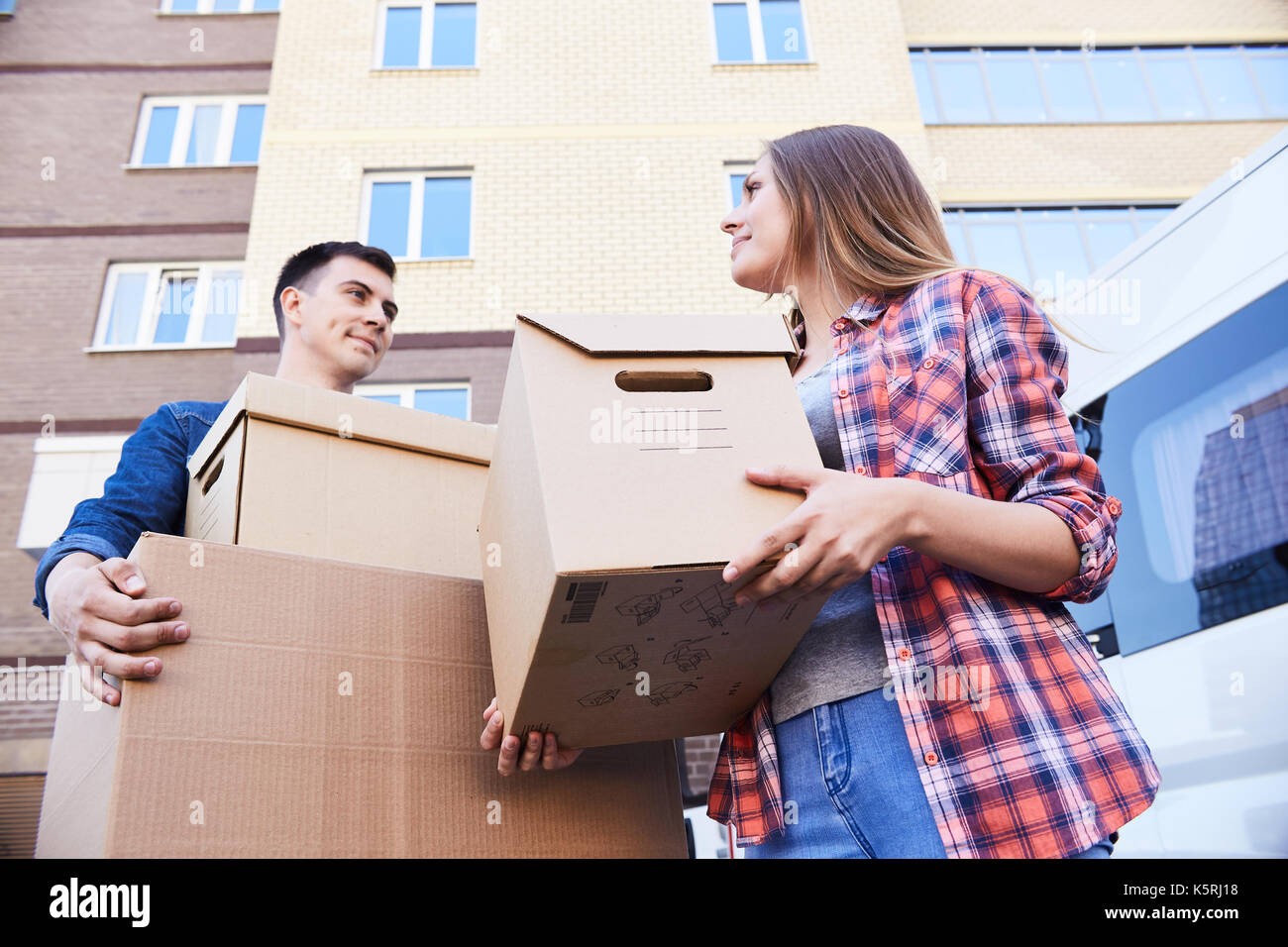 Low Angle Portrait Of Happy Couple Holding Cardboard Boxes While Moving