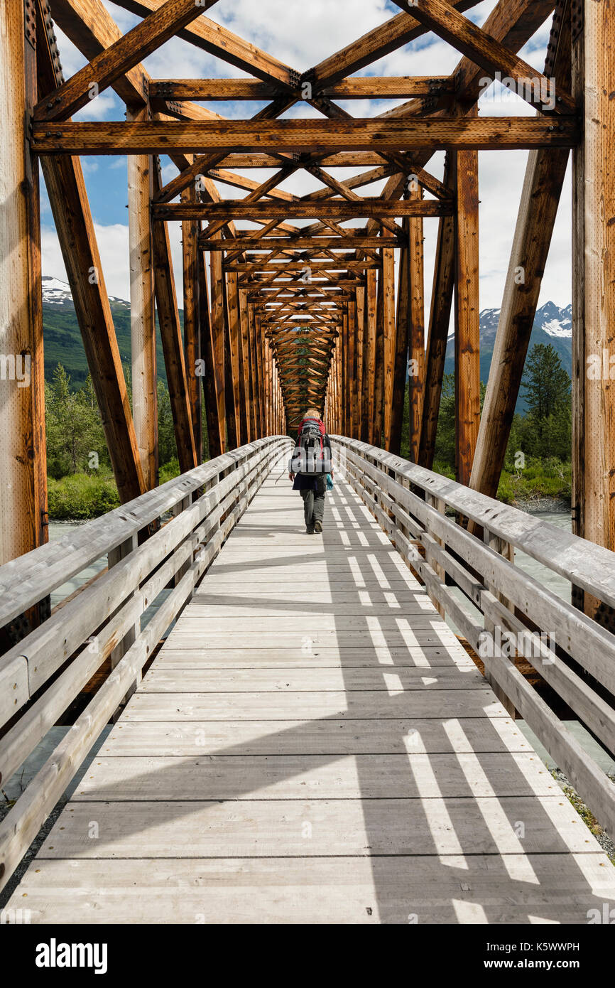 Backpacker crossing foot bridge over Placer River in Chugach National ...
