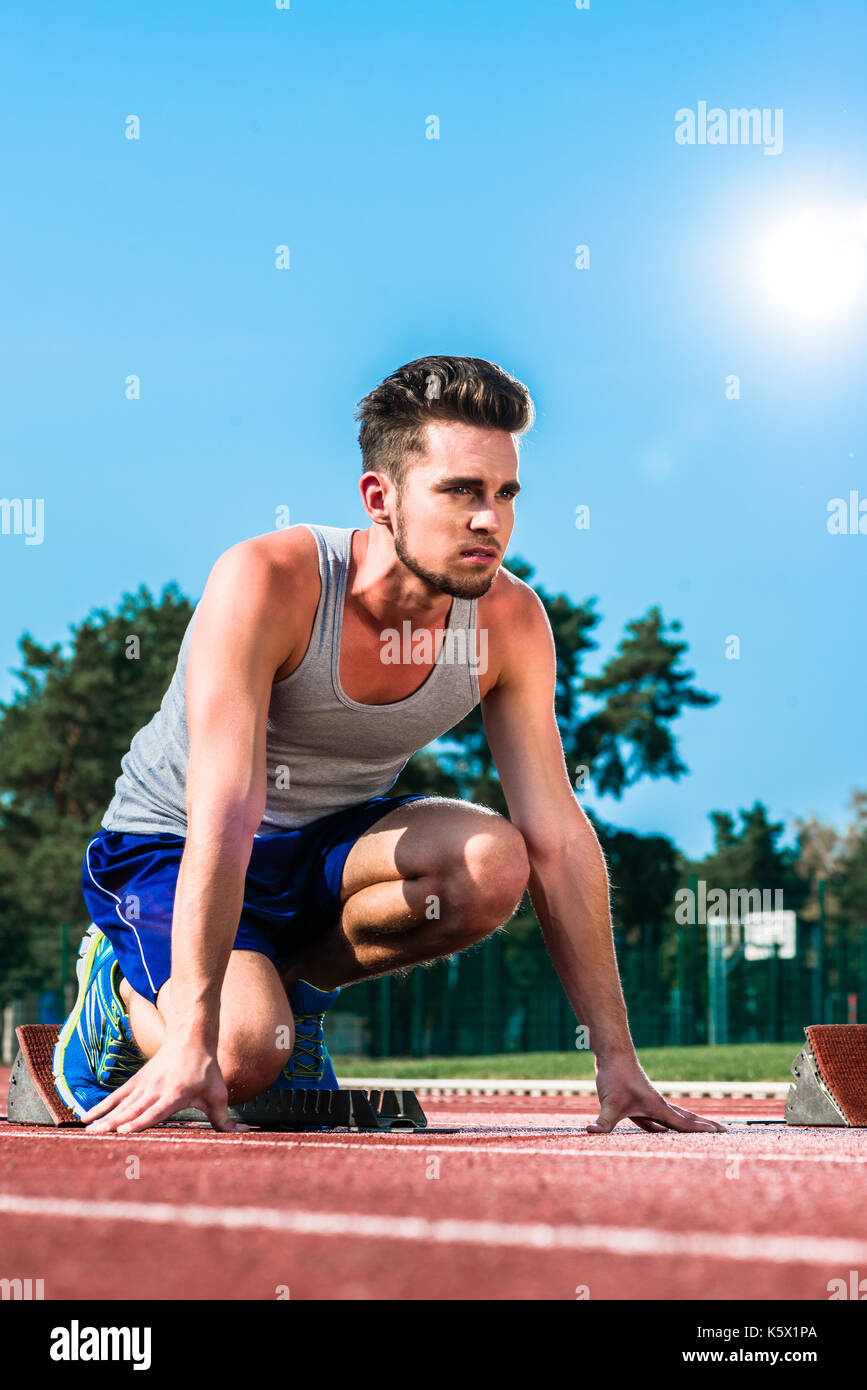 Track and field sprinter on starting point at cinder track in sports ...