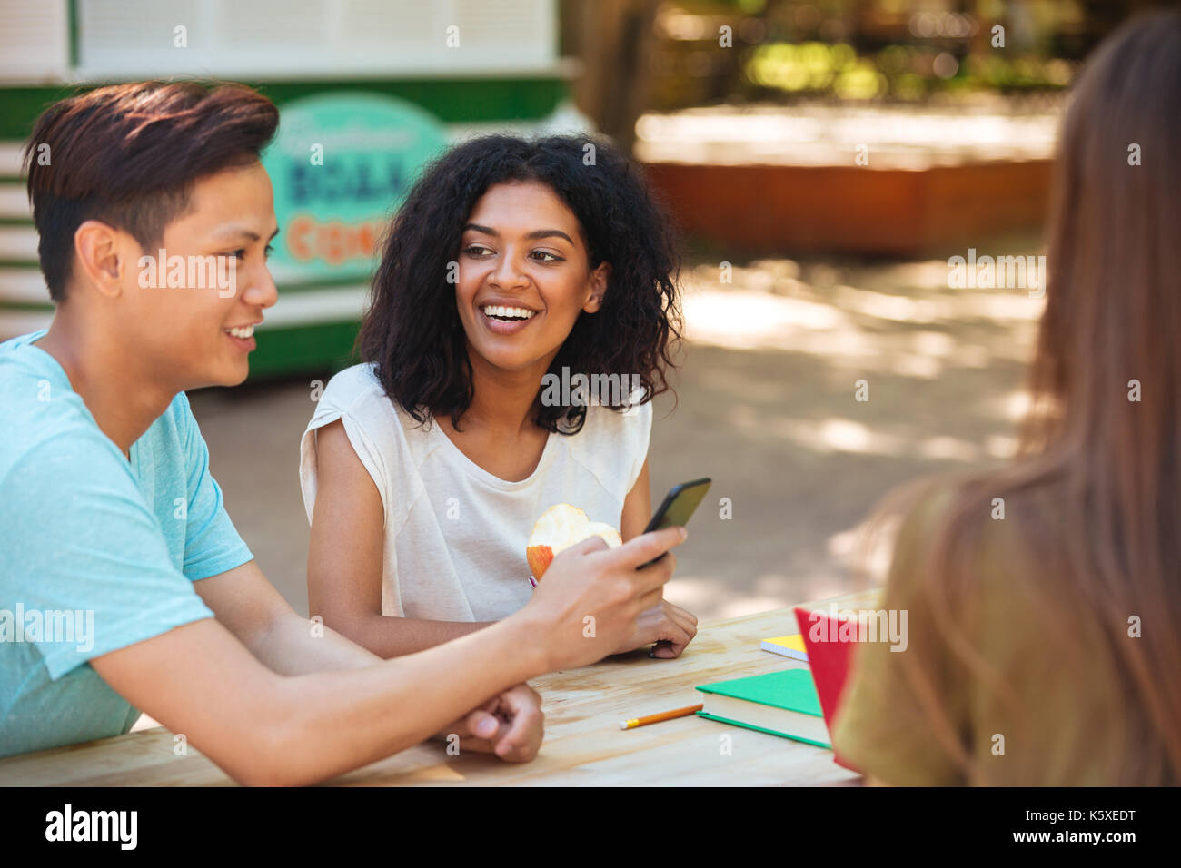 Side view of happy three friends sitting by the table outdoors Stock ...