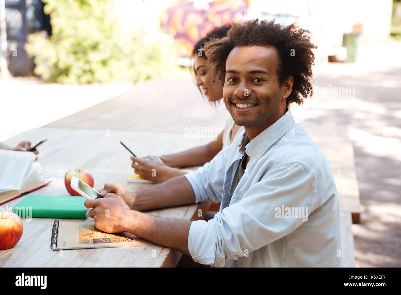 Side view of african man sitting by the table outdoors with his friends ...