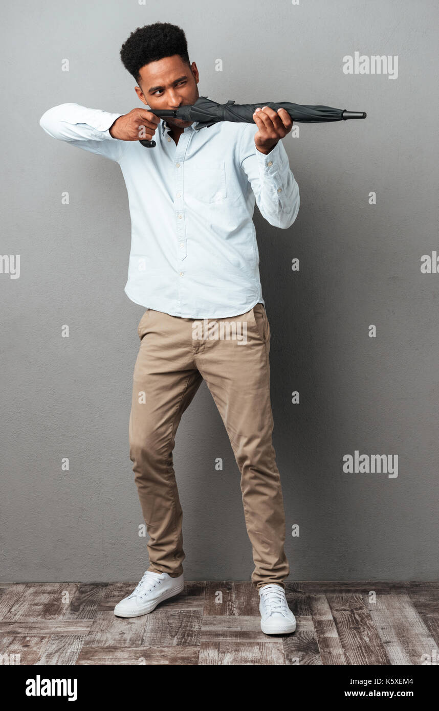 Young afro american man using umbrella like a gun and shooting isolated ...