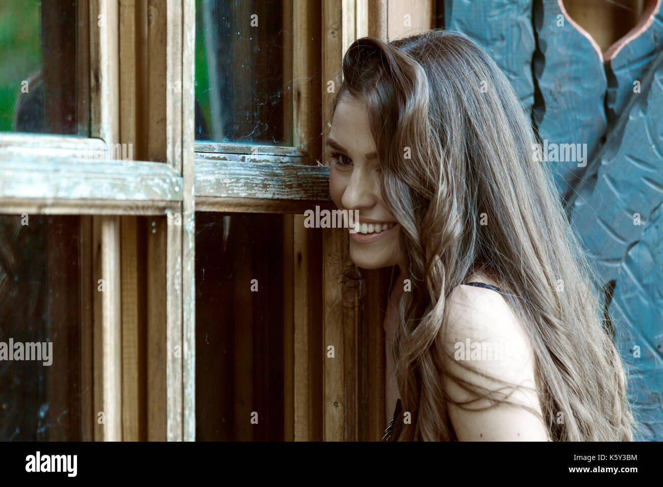Beautiful young woman standing by the window. She is happy and smiling ...
