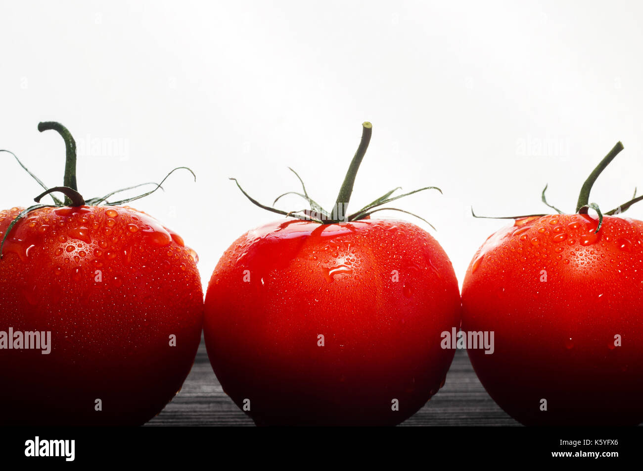 Three Red Tomatoes Standing in a Row on a Black Wooden Table Against ...