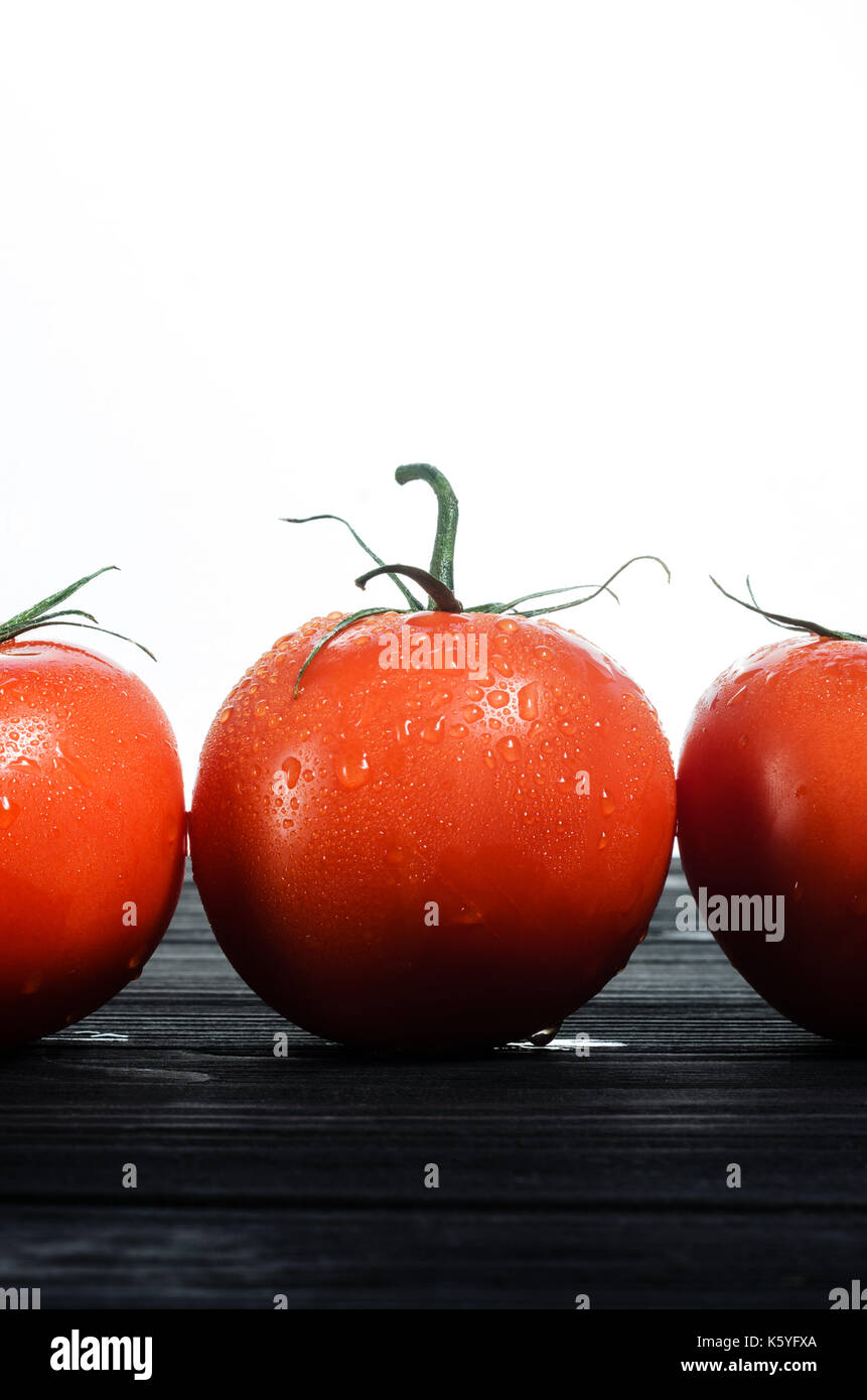 Three Red Tomatoes Standing in a Row on a Black Wooden Table Against ...