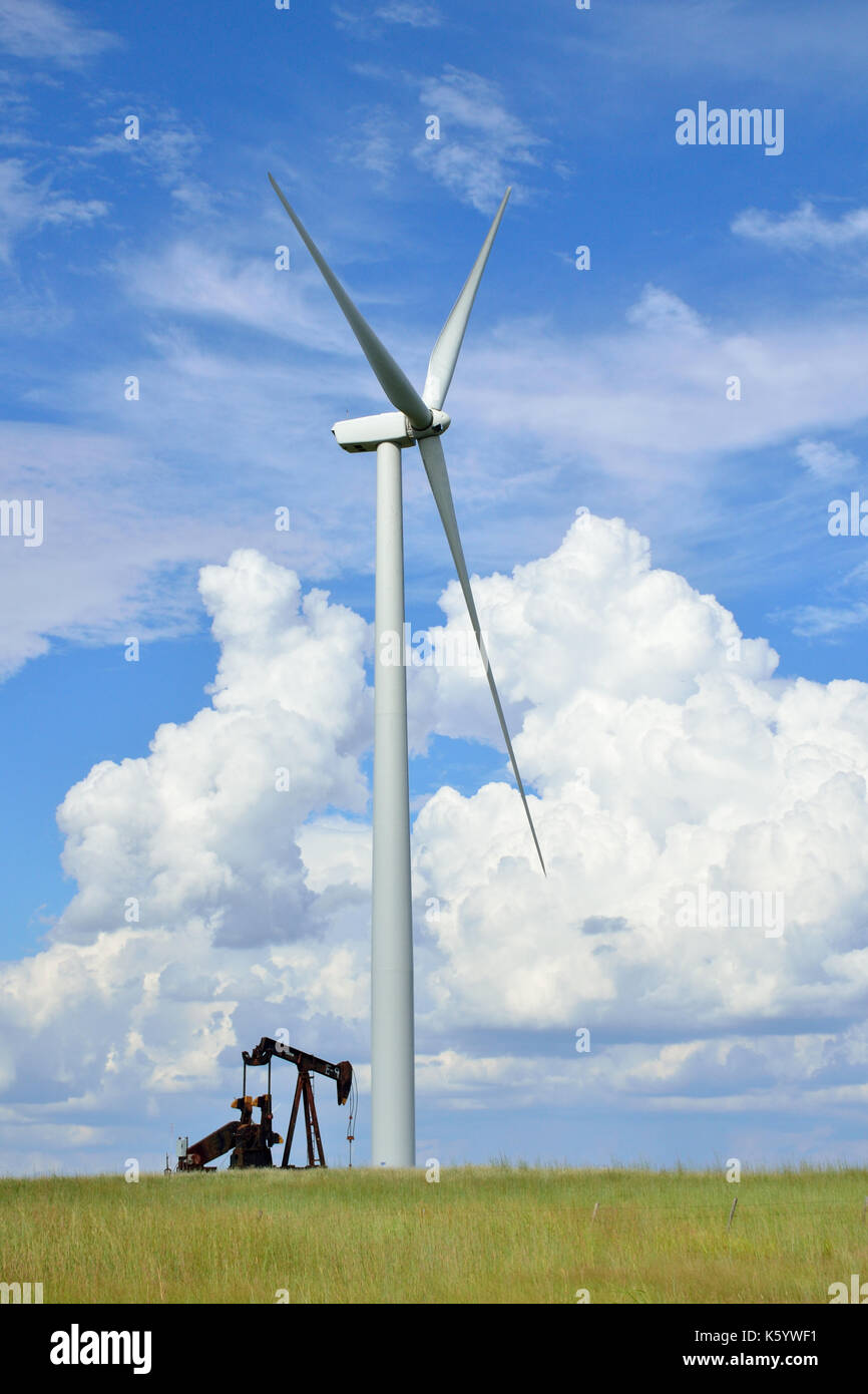 Oil pump jack in comparison to giant wind turbine against a blue ...