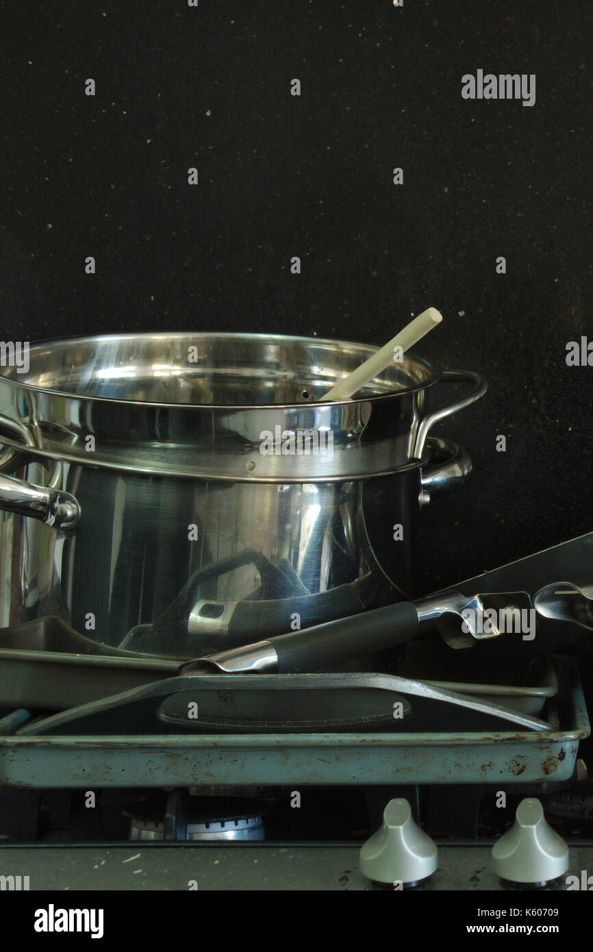 A vertical image of a pile of dirty pans stacked on a greasy gas stove ...