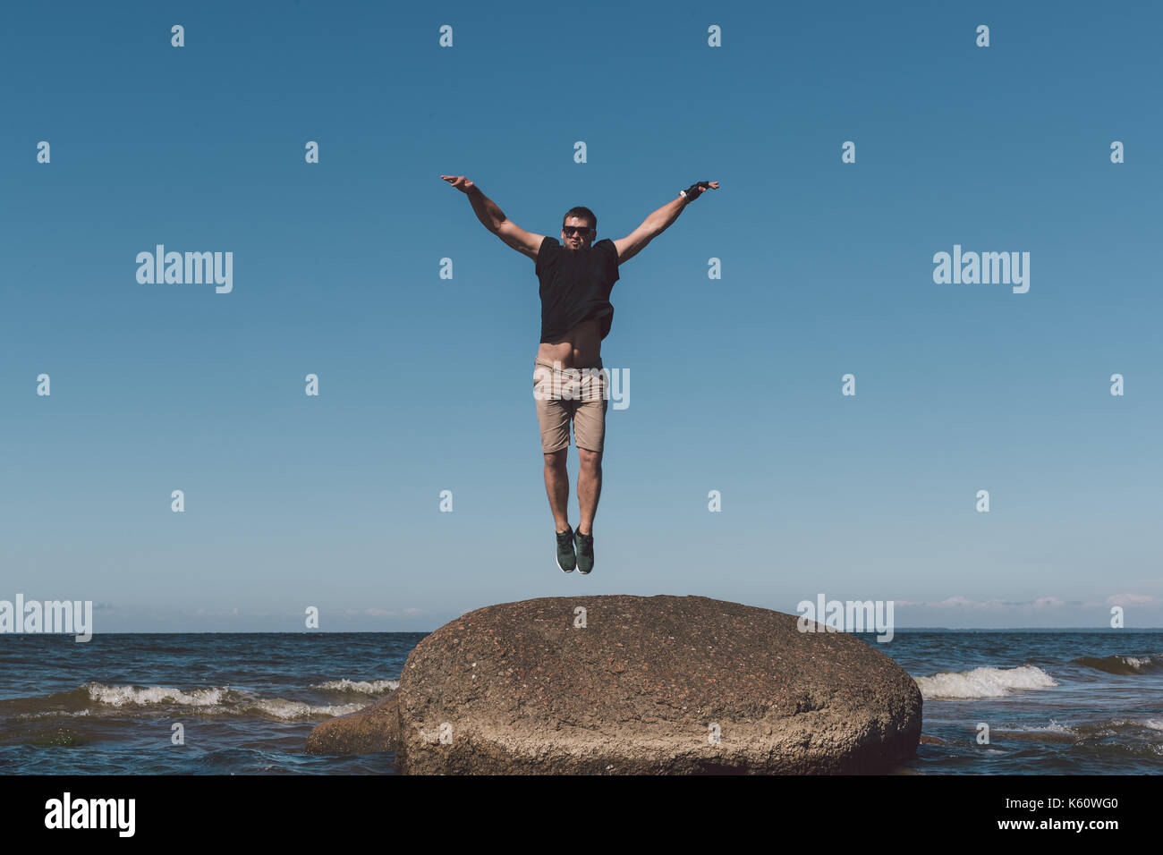 Strong man posing on a stone against a background of a bay and the sky ...