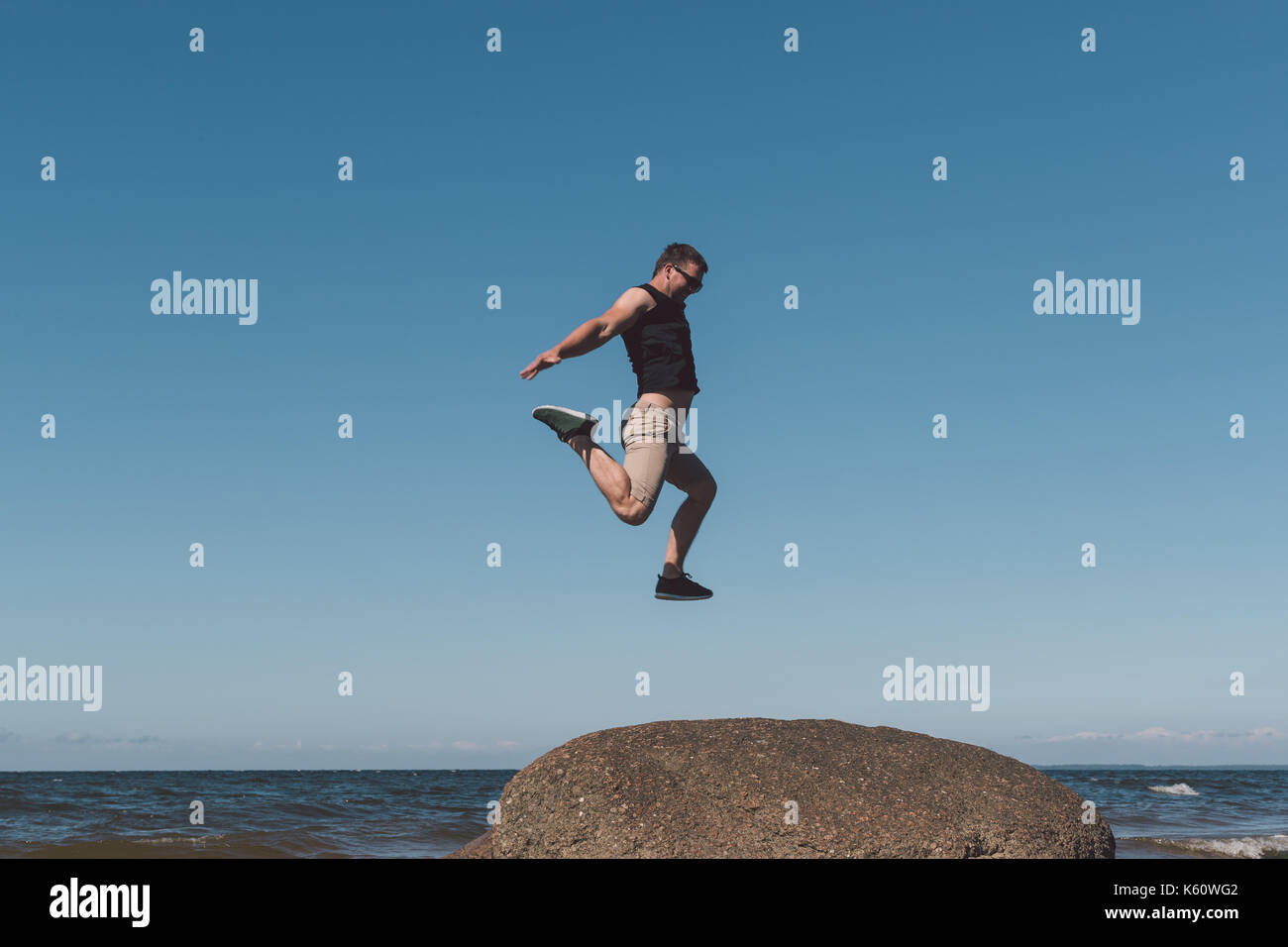 Strong man posing on a stone against a background of a bay and the sky ...