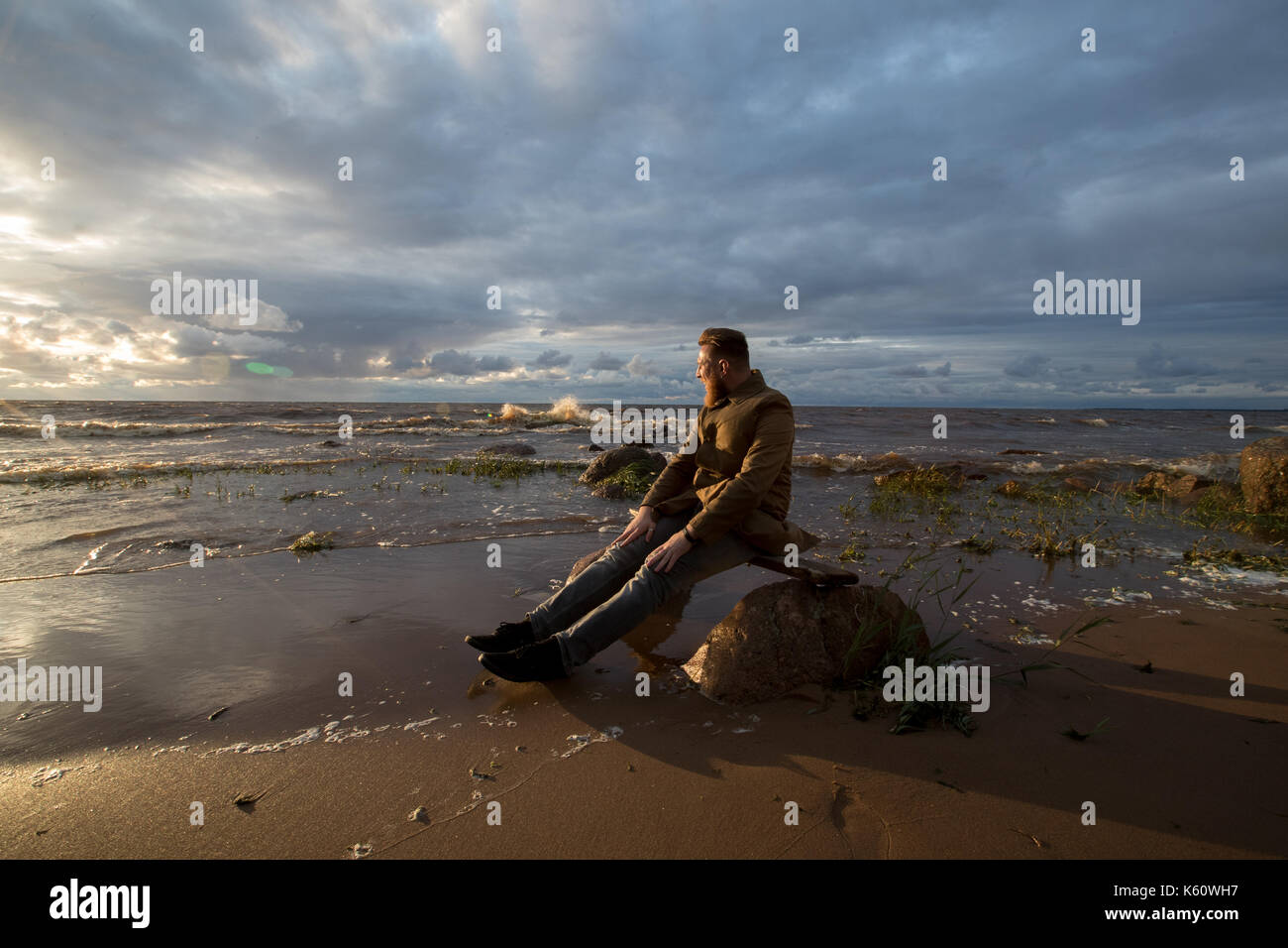 bearded guy sitting on the beach at sunset Stock Photo - Alamy