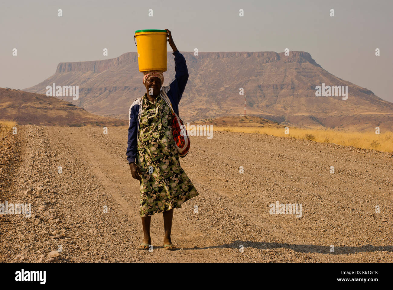 African woman carrying a bucket full of water o his head at the remote ...