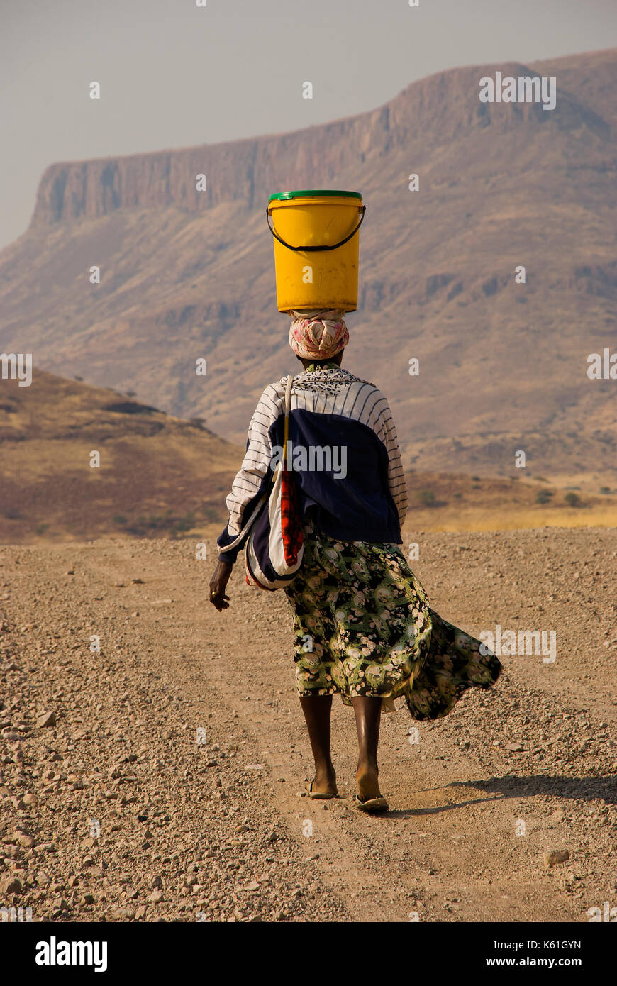 African woman carrying a bucket full of water o his head at the remote ...