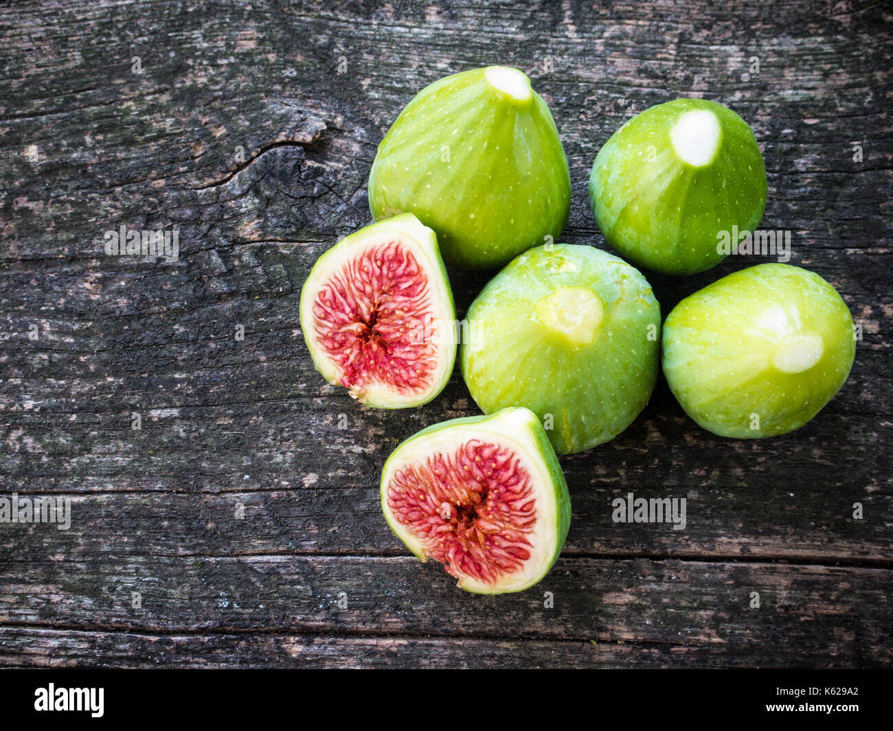 Five fresh green figs on a wooden table with one halved fig Stock Photo ...