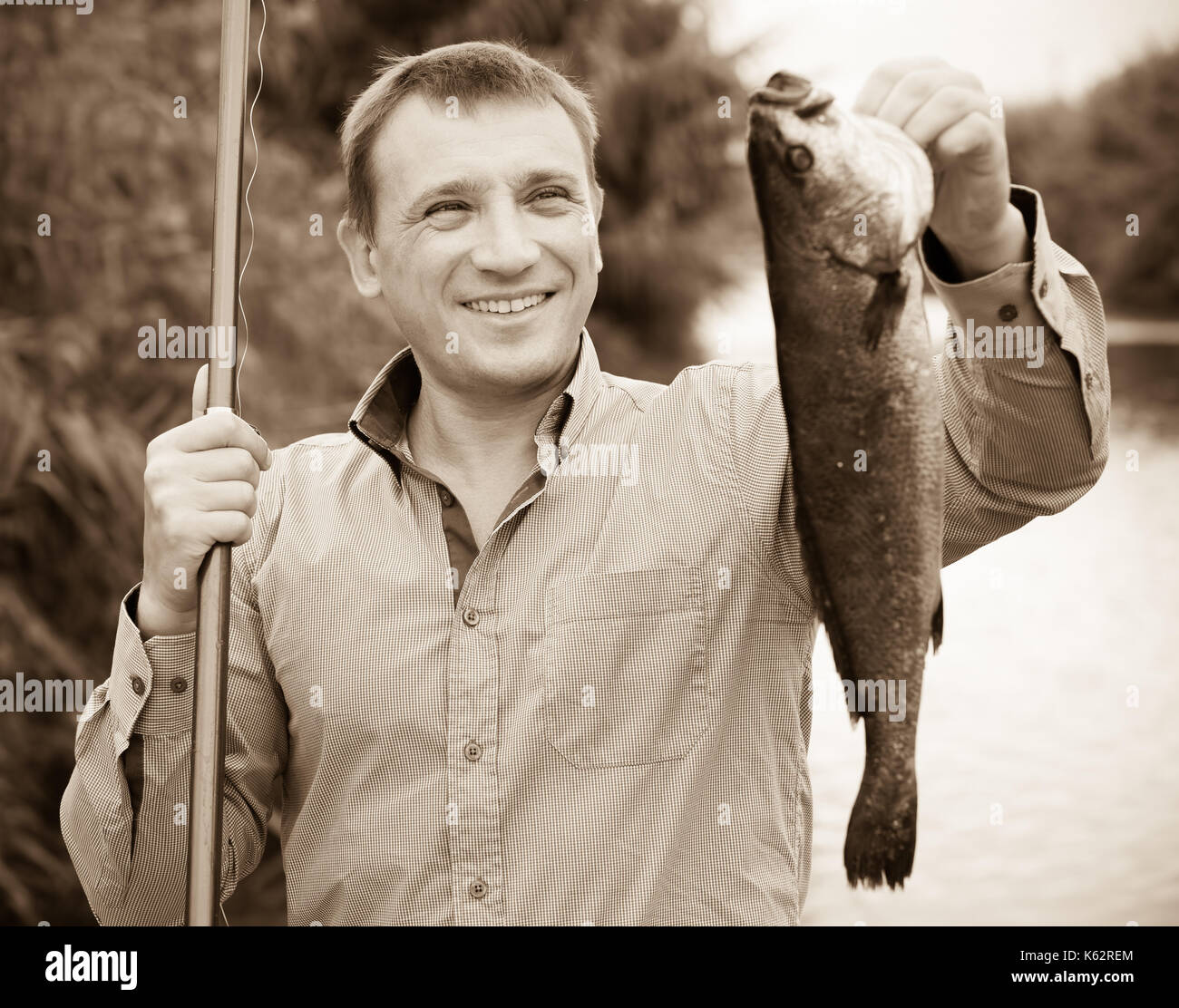 Glad man holding a fish after fishing on river side Stock Photo - Alamy